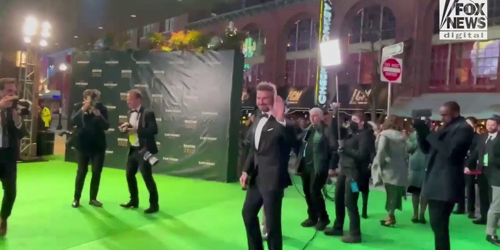 David Beckham waves to fans while walking the green carpet at the ...